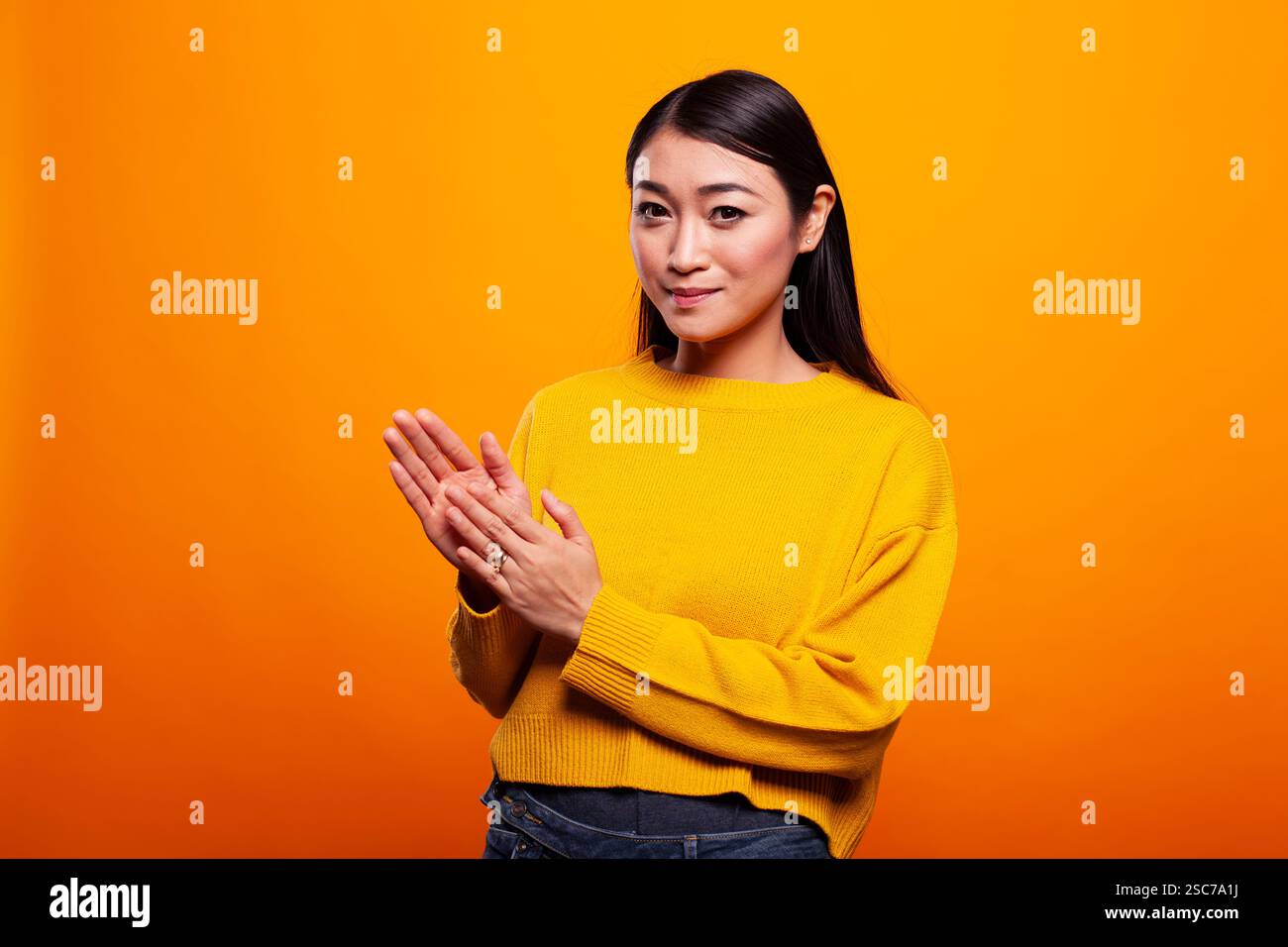 Asian woman with proud expression clapping her hands, standing against ...