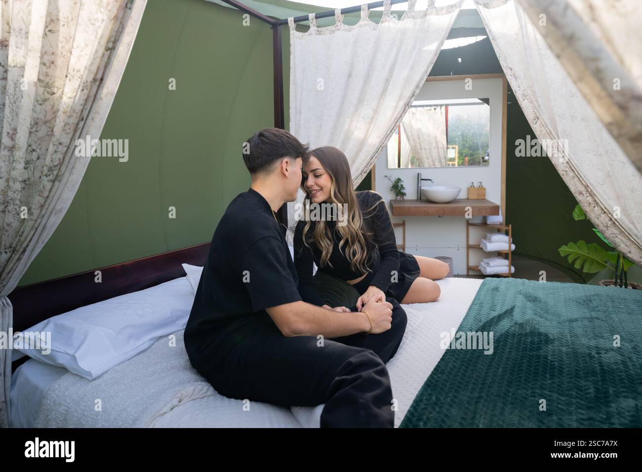 Young couple holding hands and enjoying an intimate moment together while sitting on bed inside ...