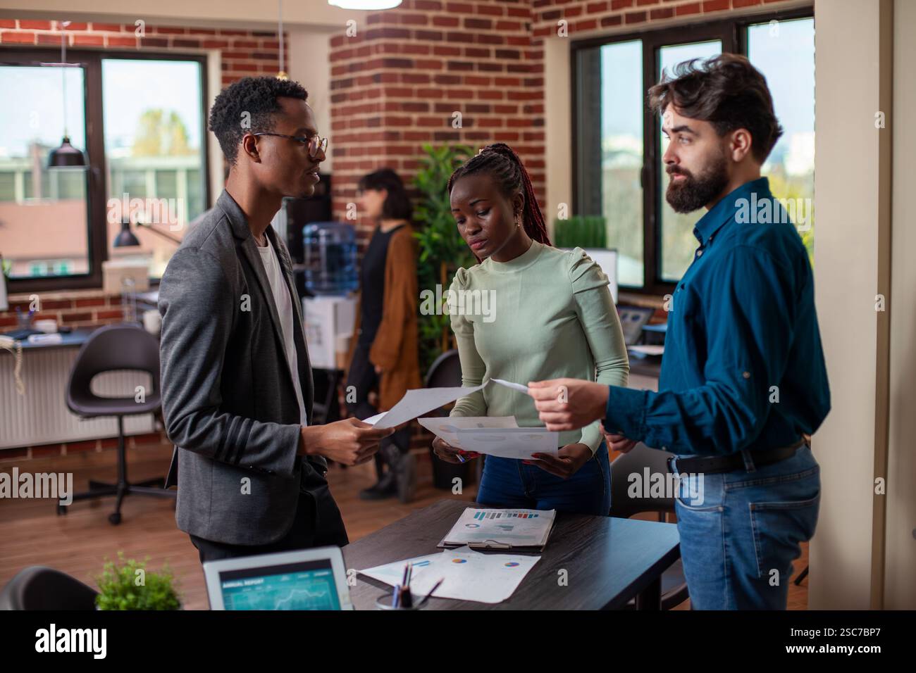 Coworkers standing around table and discussing strategies for company ...