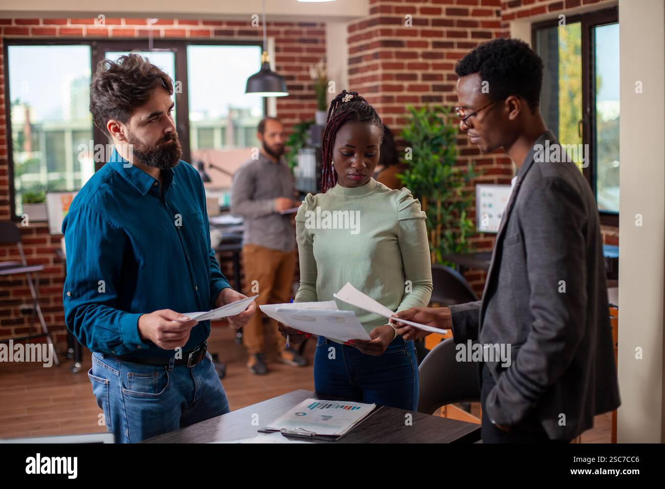 Startup employees stand around a table, reviewing company growth ideas ...