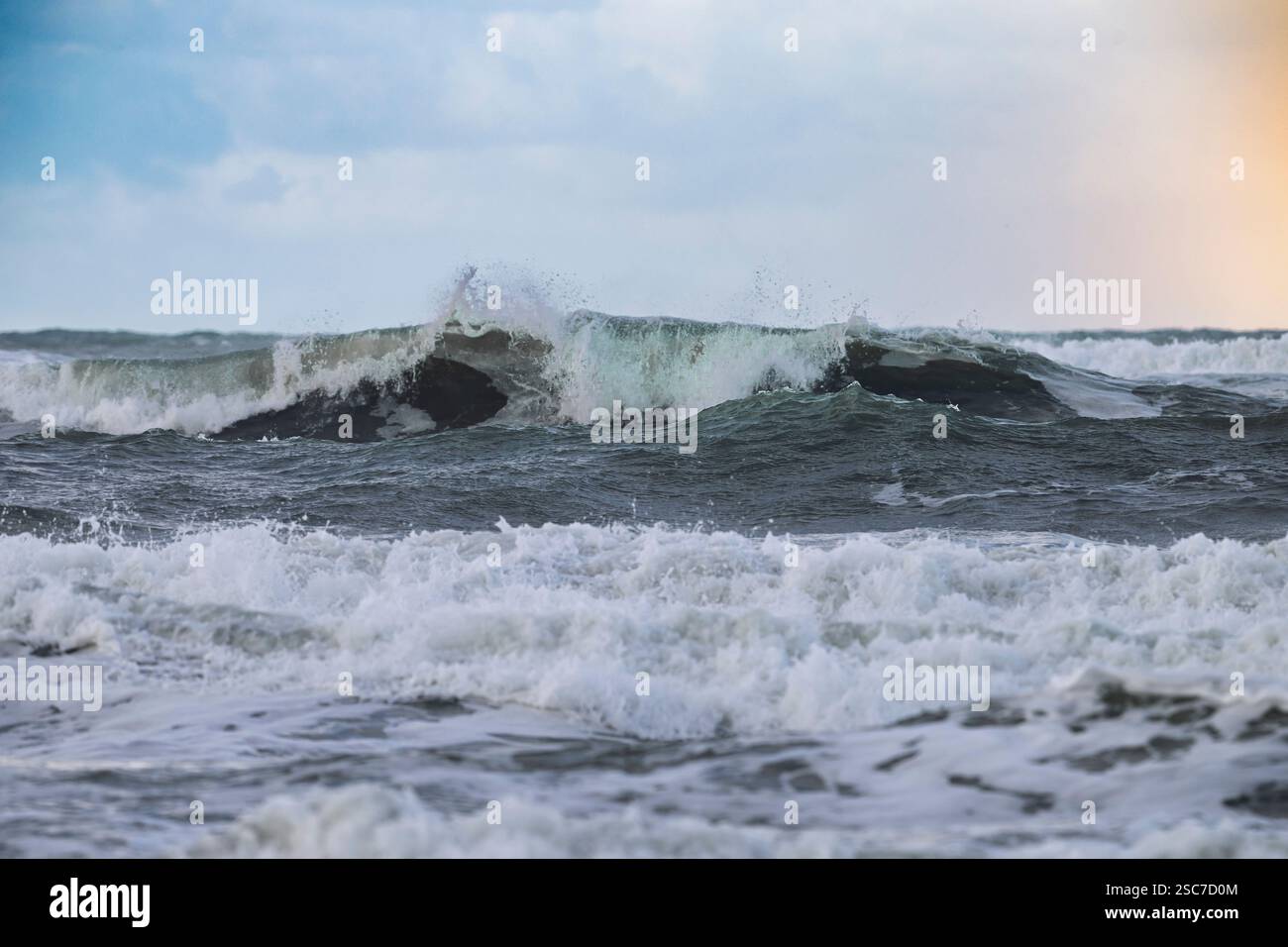 Waves crashing in a turbulent sea under a cloudy sky, creating a ...