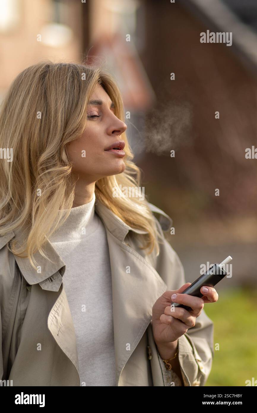 A young woman with long blonde hair stands in a park, taking a moment ...