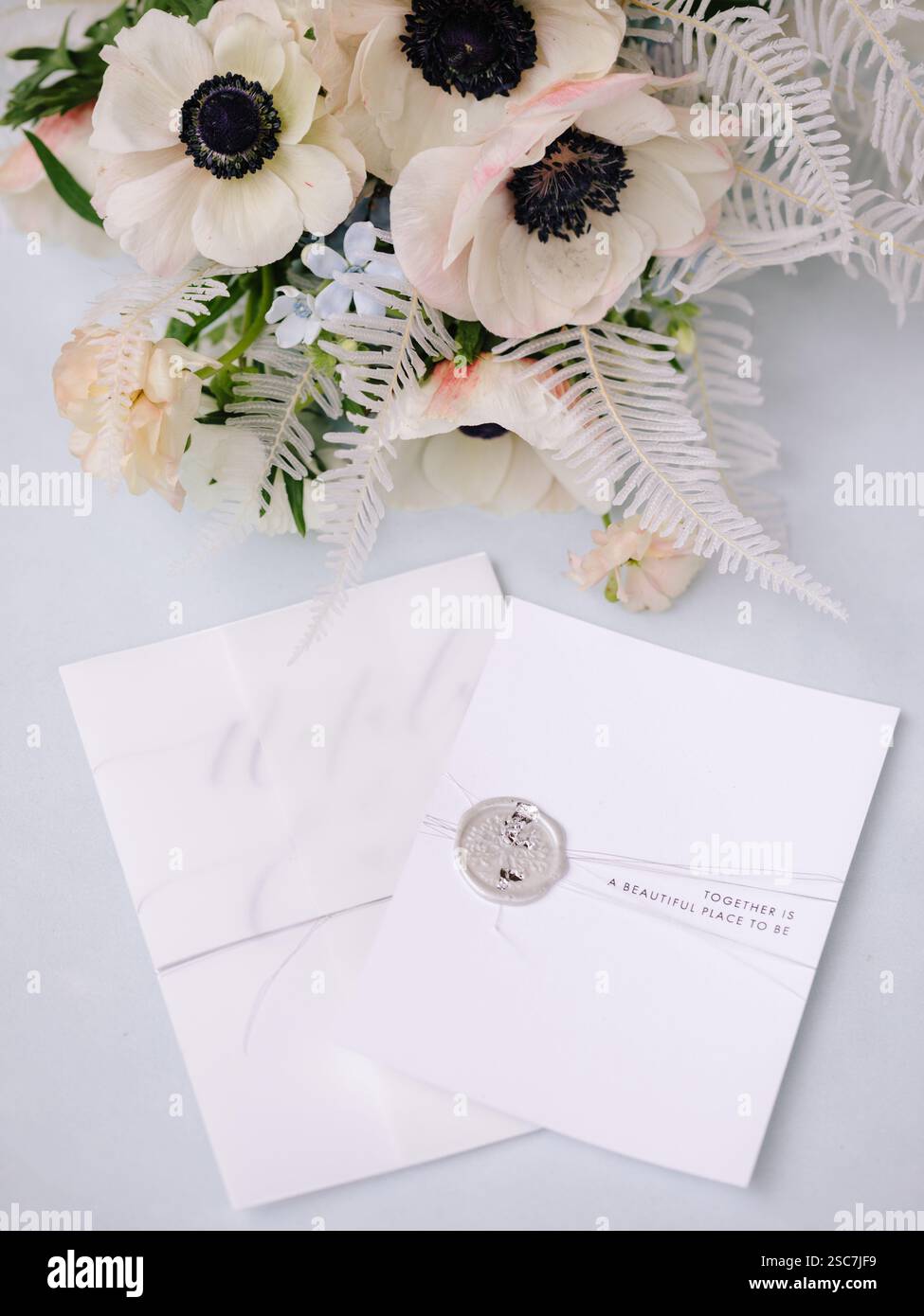 Beautiful wedding invitations are displayed next to a bouquet featuring ...
