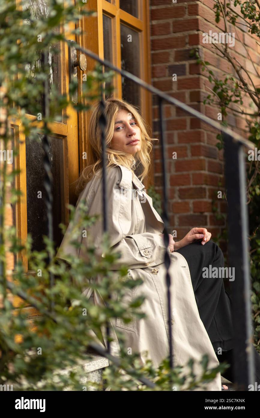 Relaxing on the steps of a charming brick house, a young woman with ...