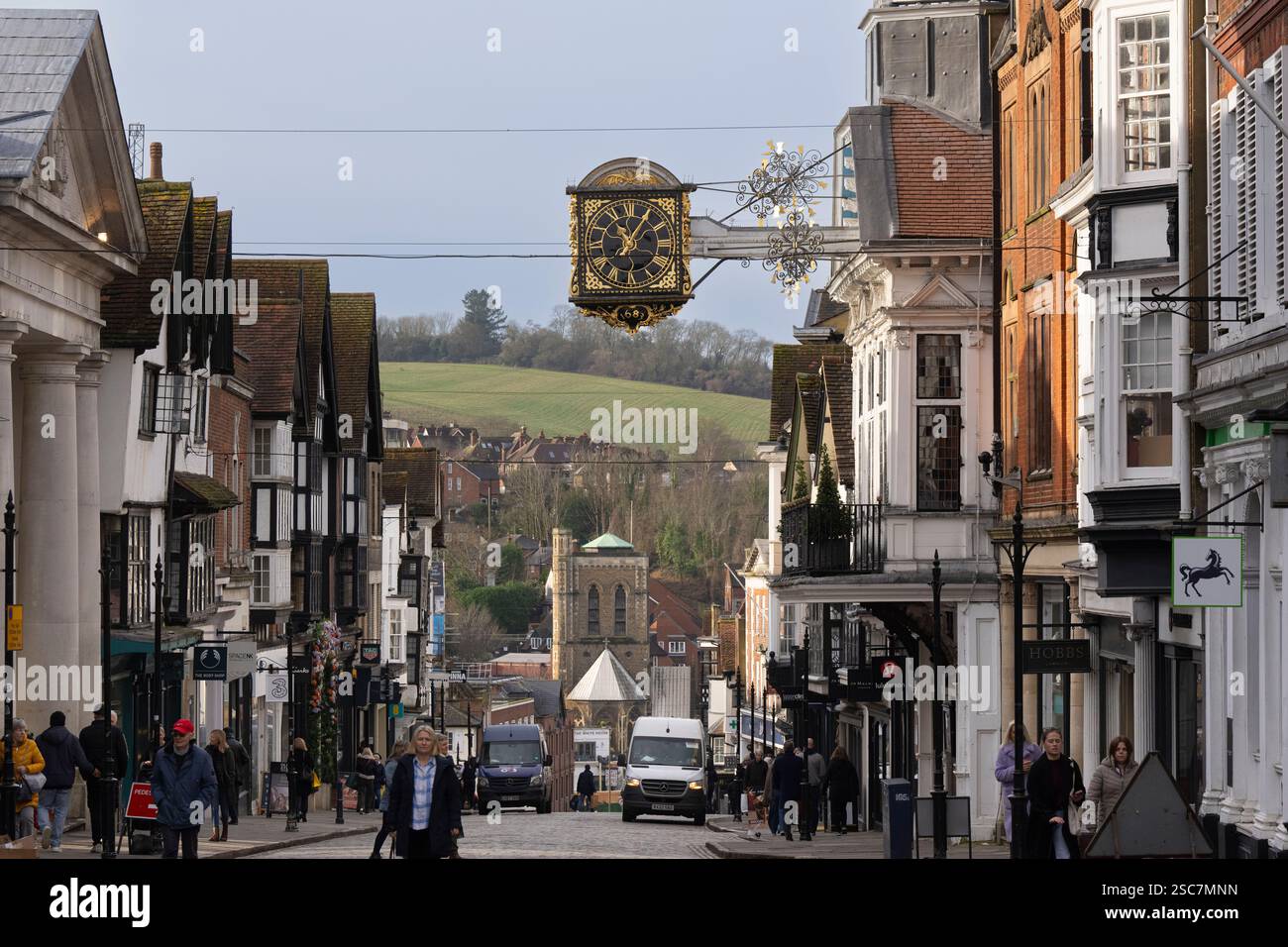 Pedestrians walk along High Street, Guildford, UK. A historic clock ...