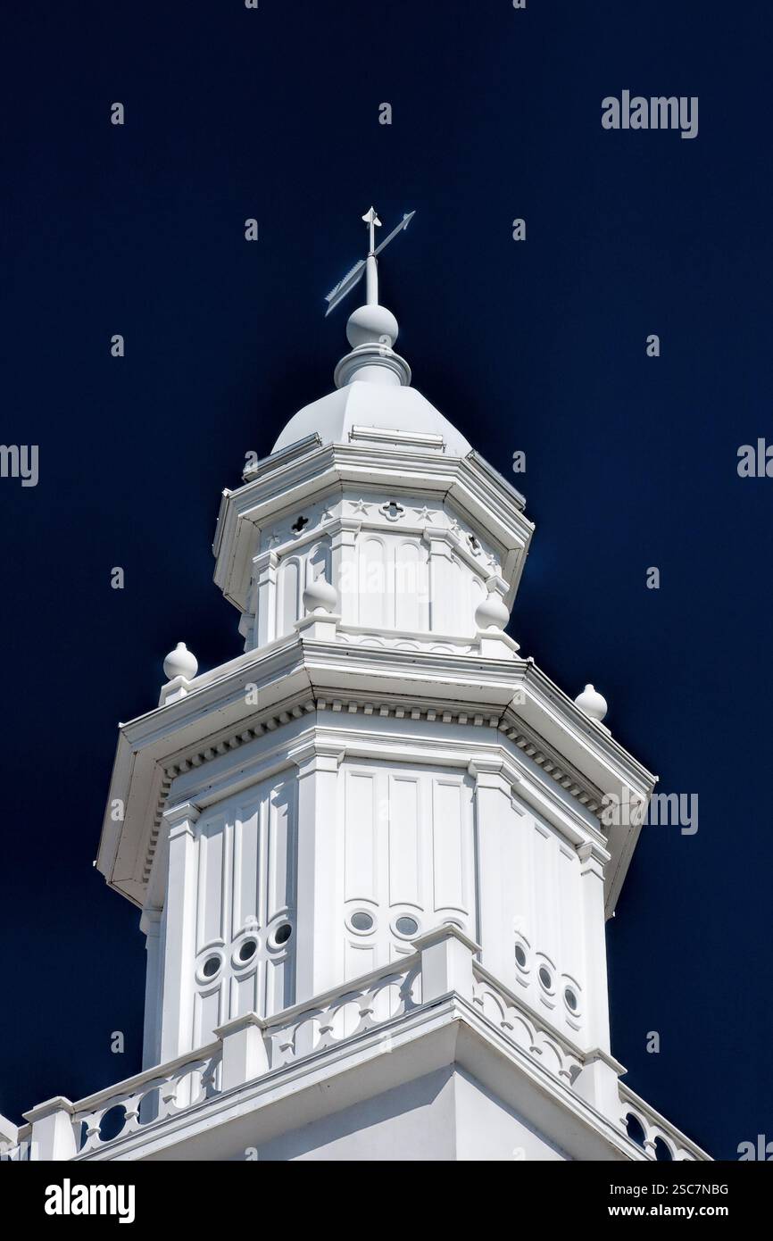 A white church steeple with a cross on top. The cross is pointing to ...