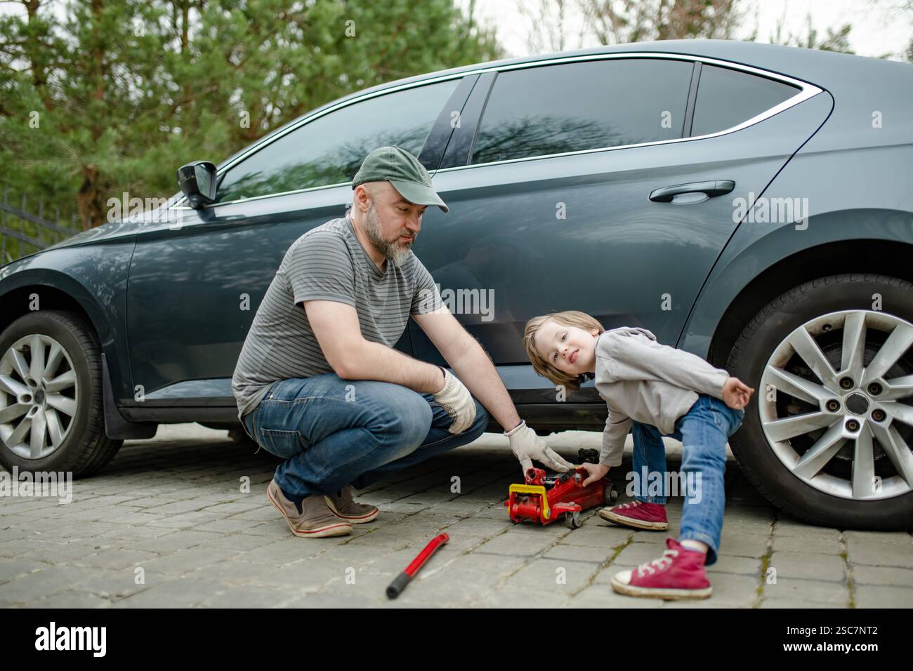 Cute little boy helping his father to change car wheels at their backyard. Father teaching his ...