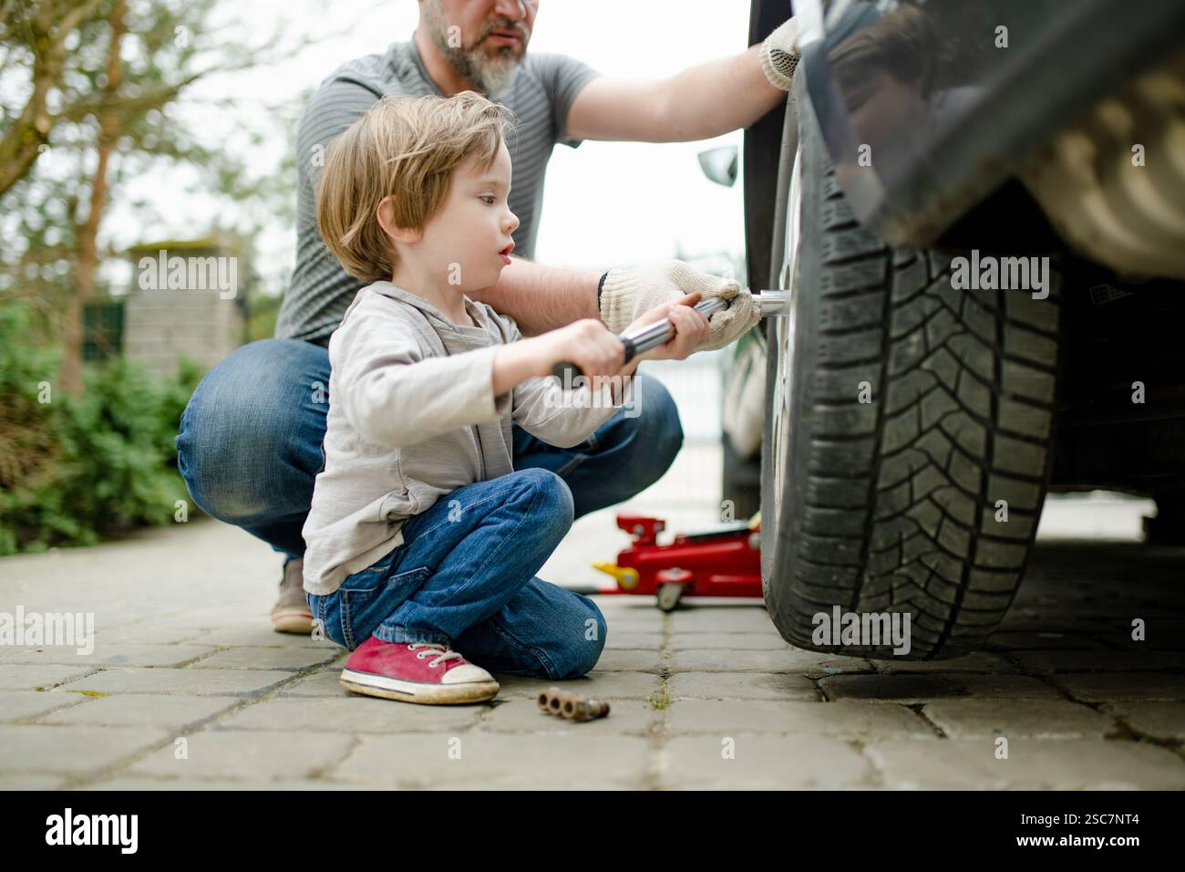 Cute little boy helping his father to change car wheels at their backyard. Father teaching his ...
