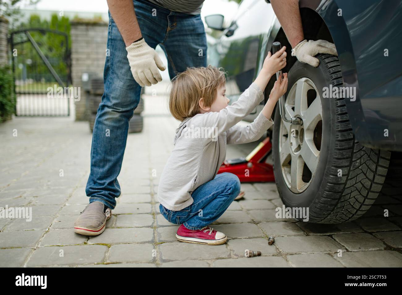Cute little boy helping his father to change car wheels at their backyard. Father teaching his ...