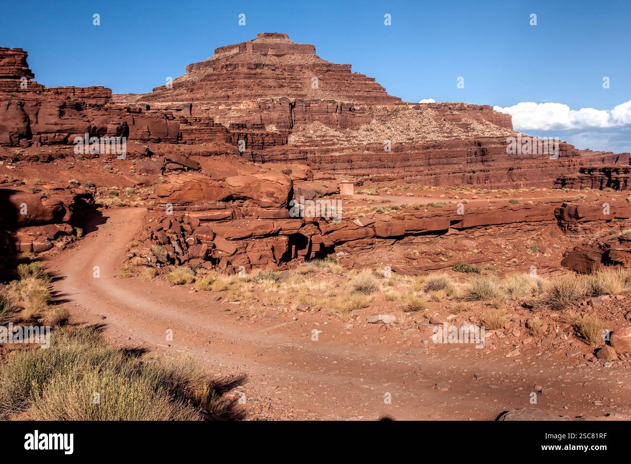 A dirt road in the desert with a large rock formation in the background ...
