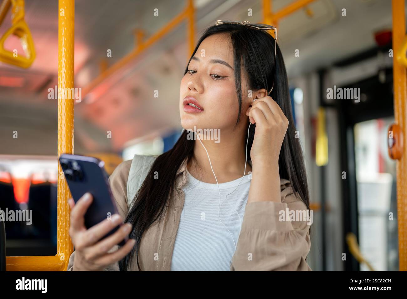 A beautiful Asian woman in casual clothes puts in her earphones ...