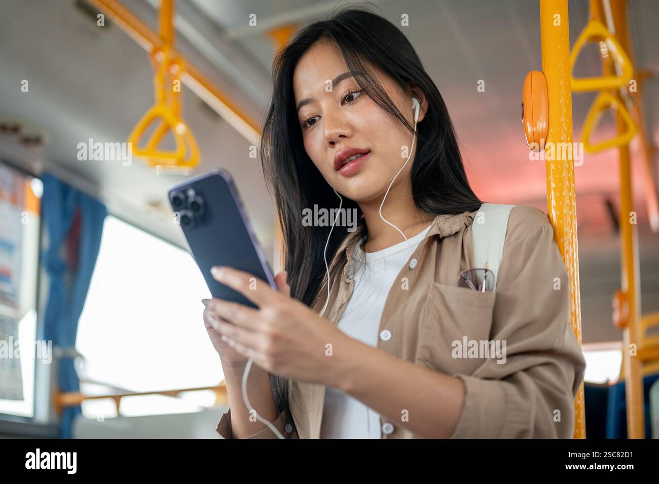 A relaxed, beautiful Asian woman in casual clothes uses her smartphone, reads text messages ...