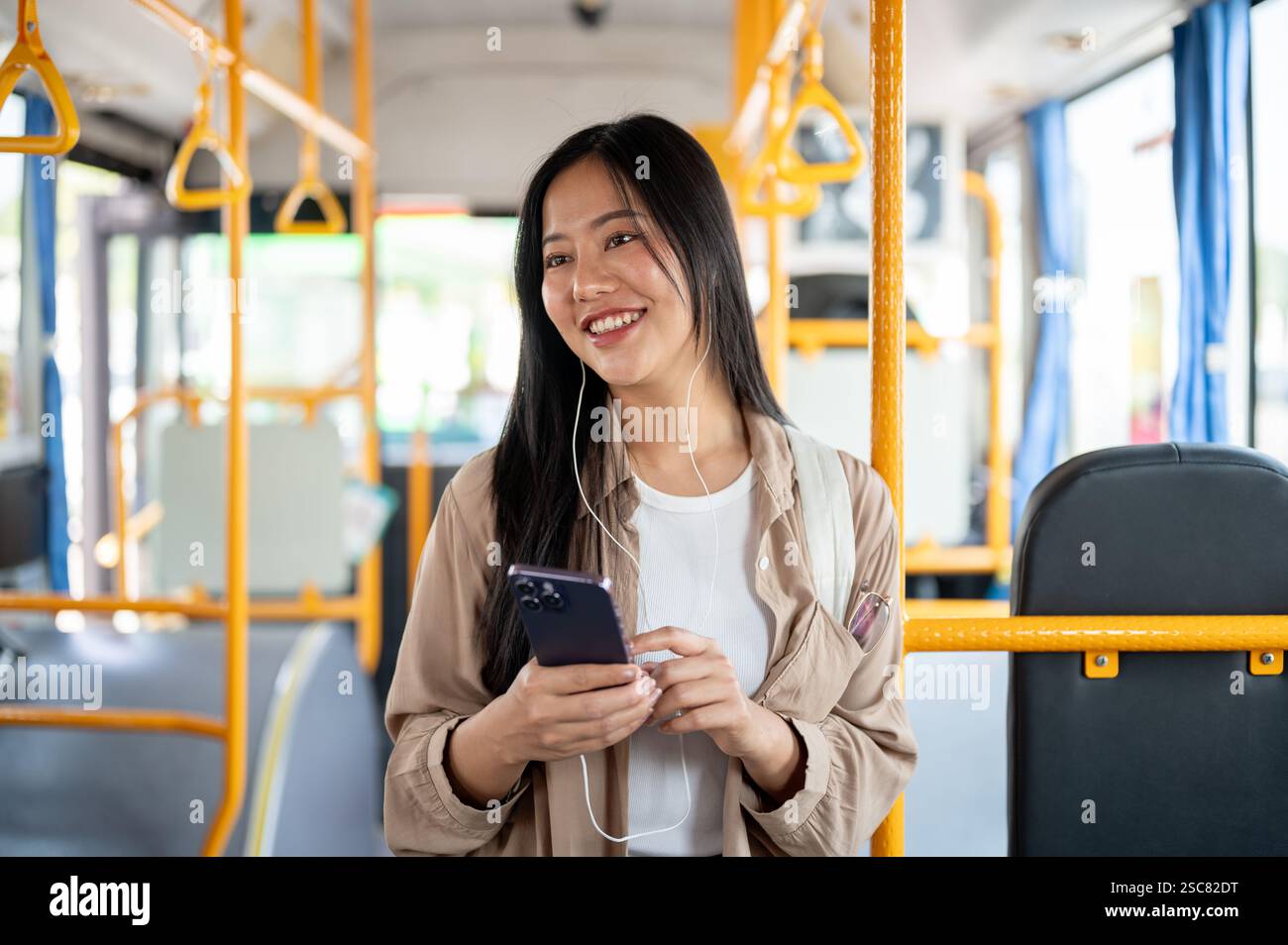 An attractive, cheerful Asian woman in casual clothes stands on a bus ...