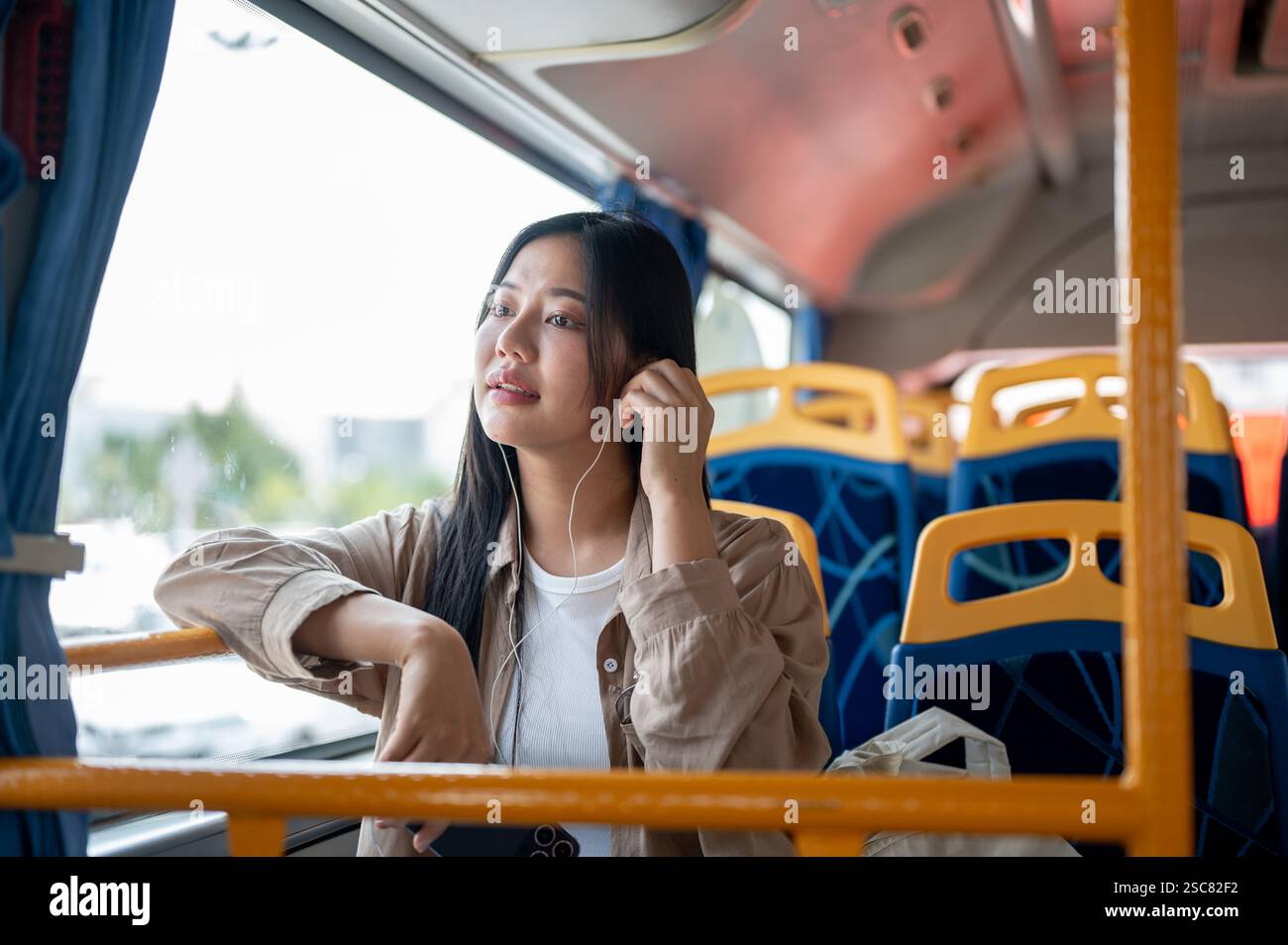 A beautiful, relaxed Asian woman in casual clothes listens to music ...
