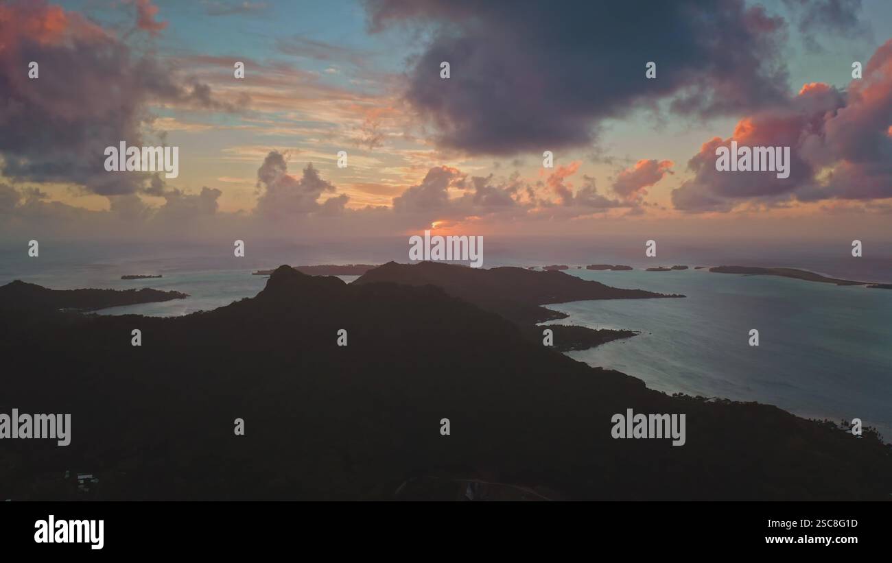 The setting sun casts a warm glow over the dramatic peaks of Bora Bora ...