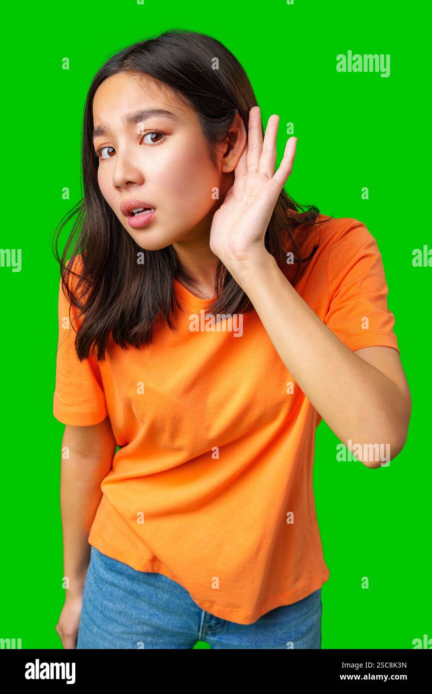 Young woman in orange shirt curiously listening against a bright green ...
