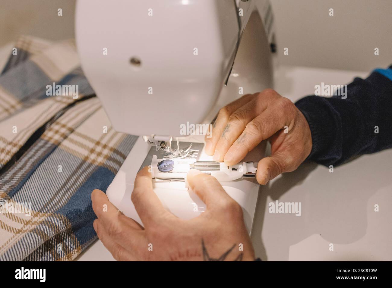 Tailor using sewing machine to sew button on checkered fabric ...
