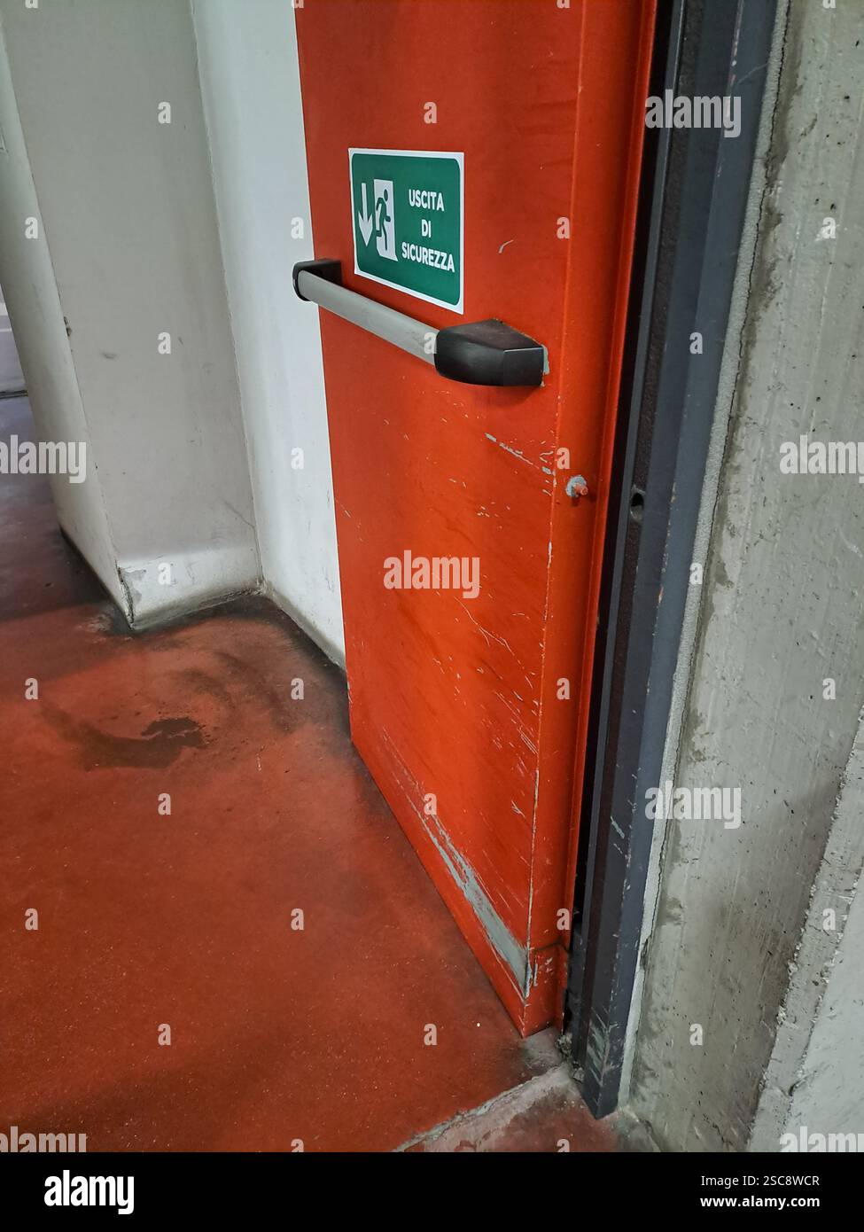 Panic bar on an open orange door. Sign with the writing in Italian ...