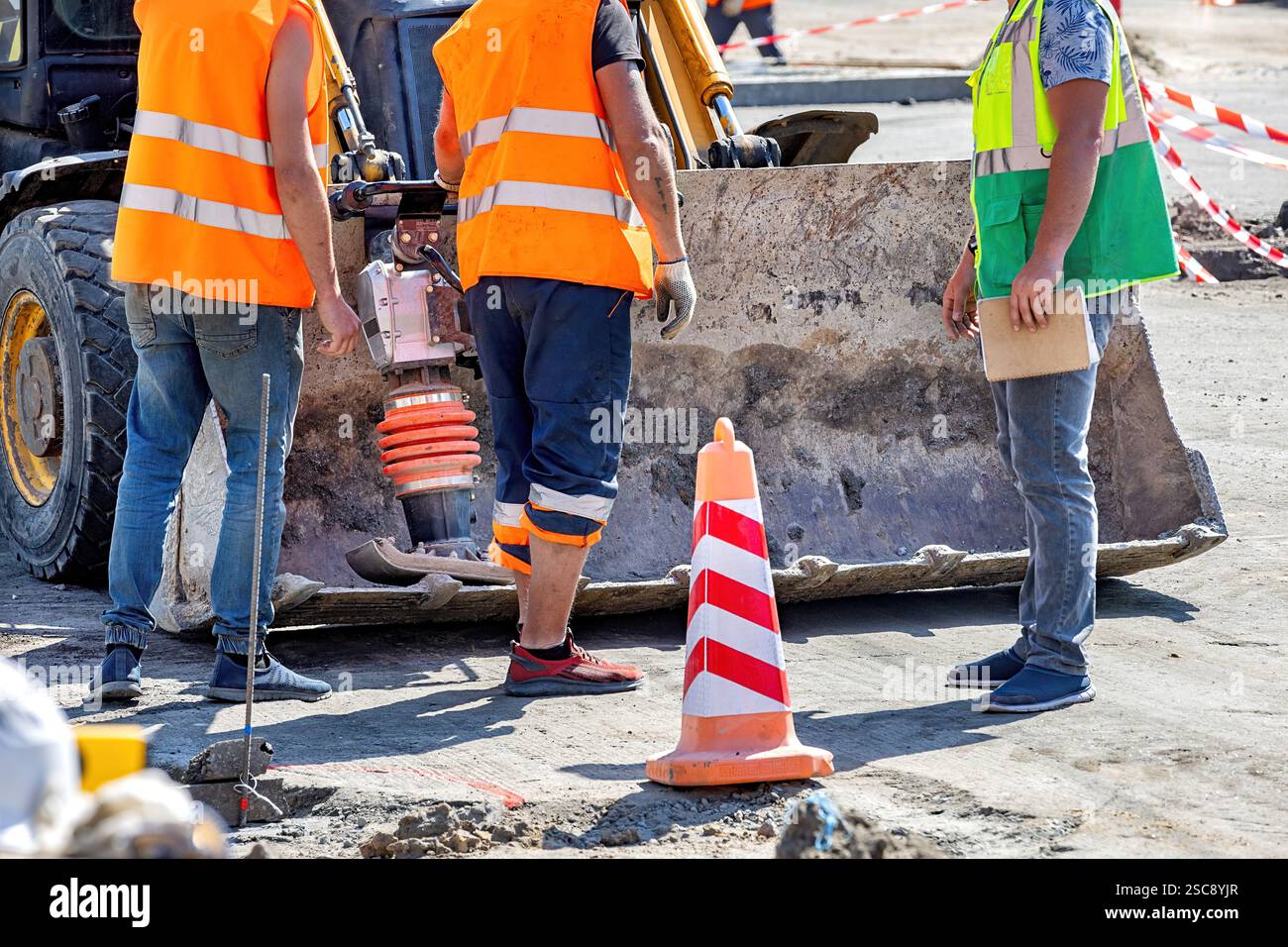 Workers in bright vests operate machinery at a construction site under ...