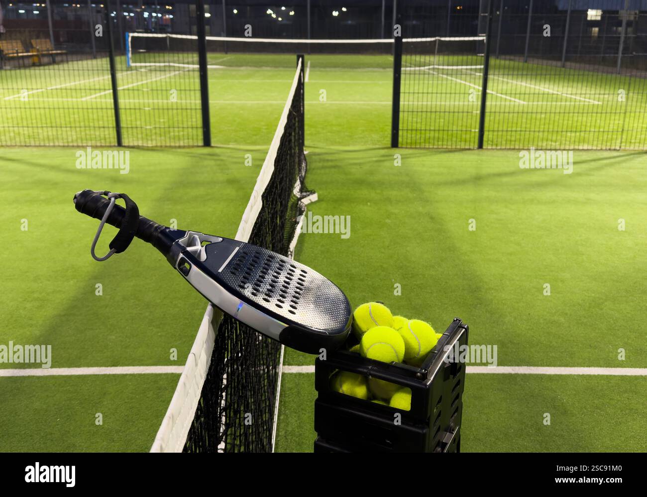 Padel racket and yellow ball behind net on a green court grass turf ...