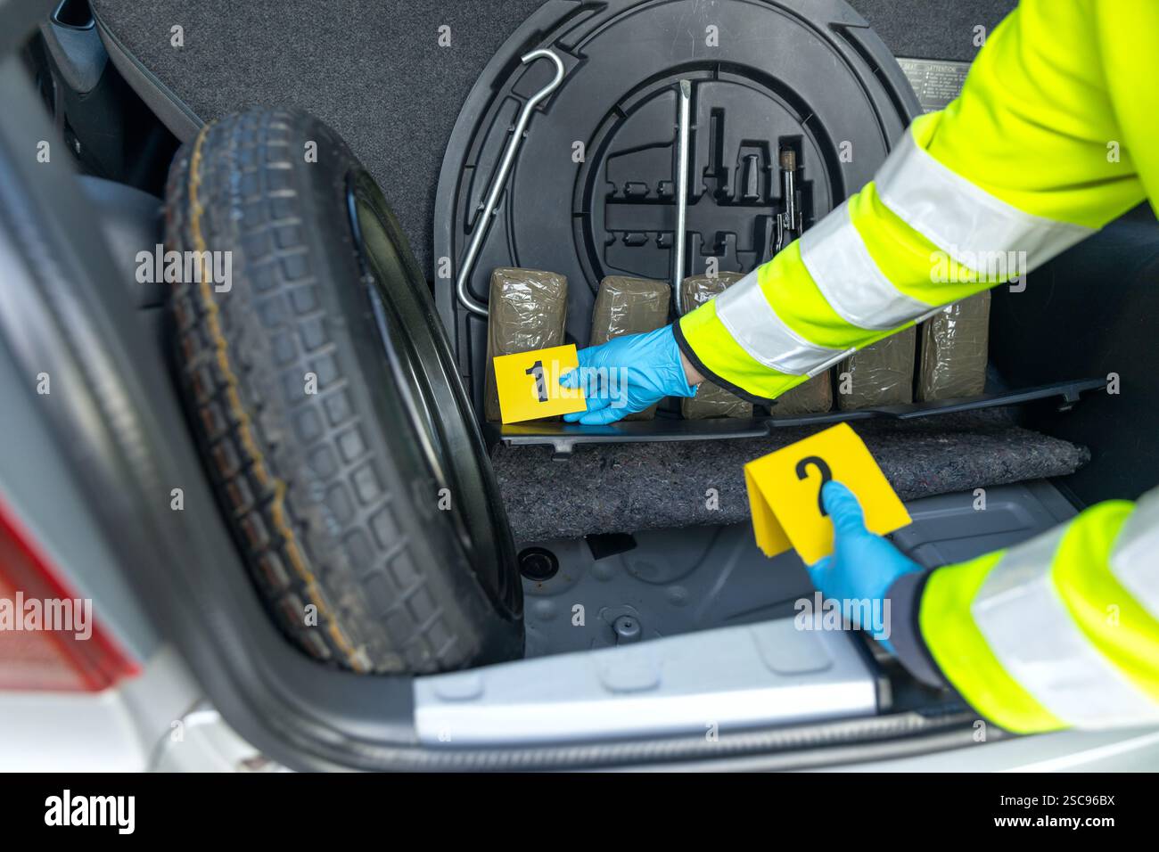 Police officer investigating drug packages hidden in a car trunk with ...