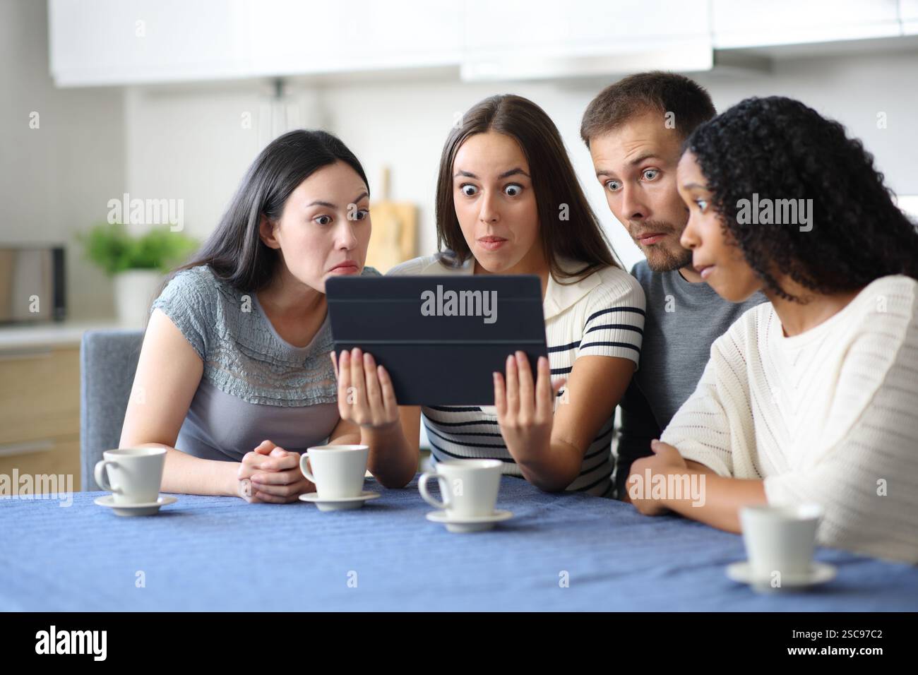 Perplexed group of friends checking tablet in the kitchen at home Stock ...