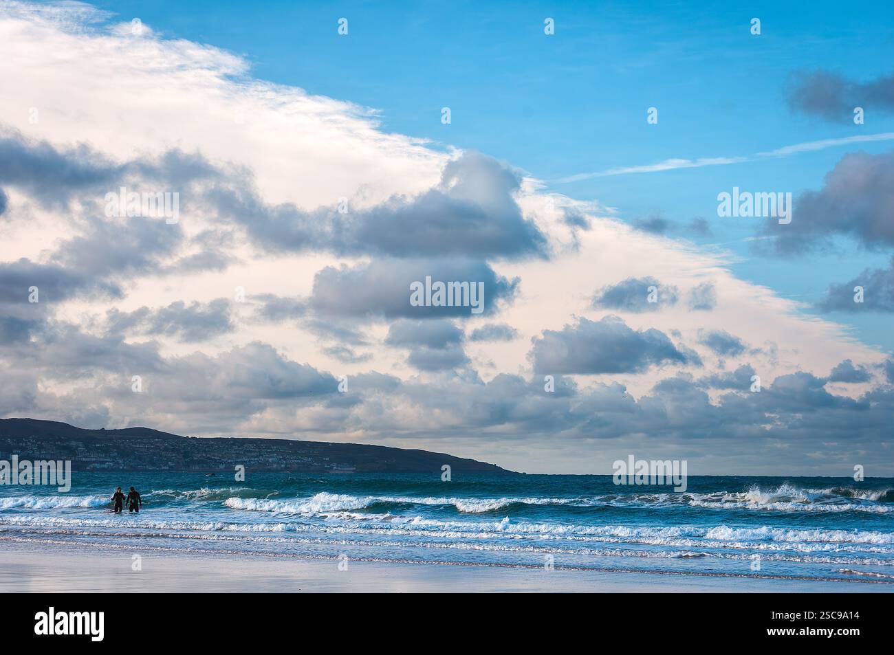 Two surfers, likely in wetsuits, are wading in the waves at the ...