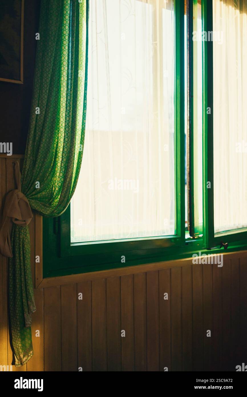 A view of an old green window and a green curtain tied in a decorative ...