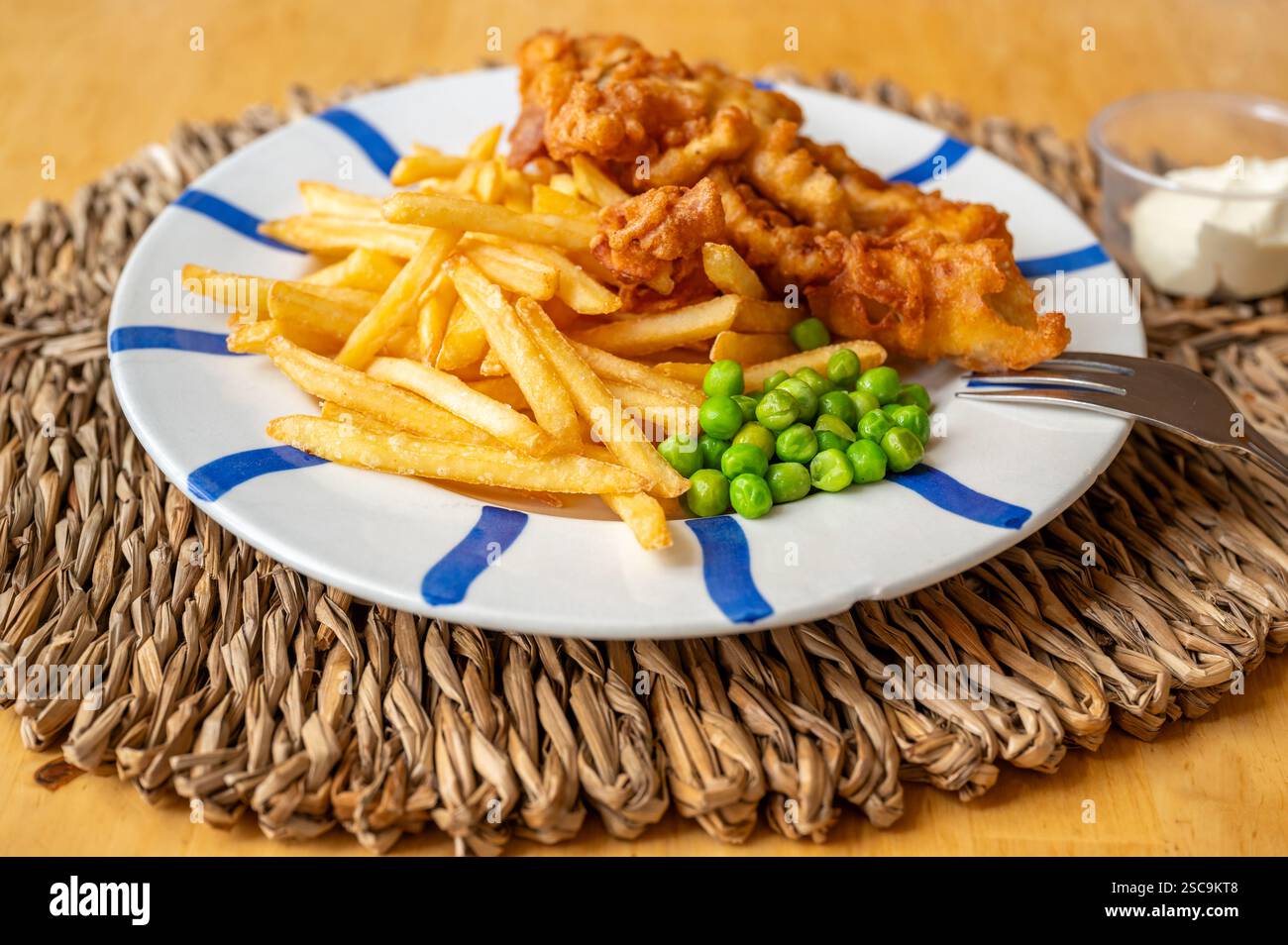 Fish and chips and pea on striped plate, fork, mayonnaise in small bowl ...