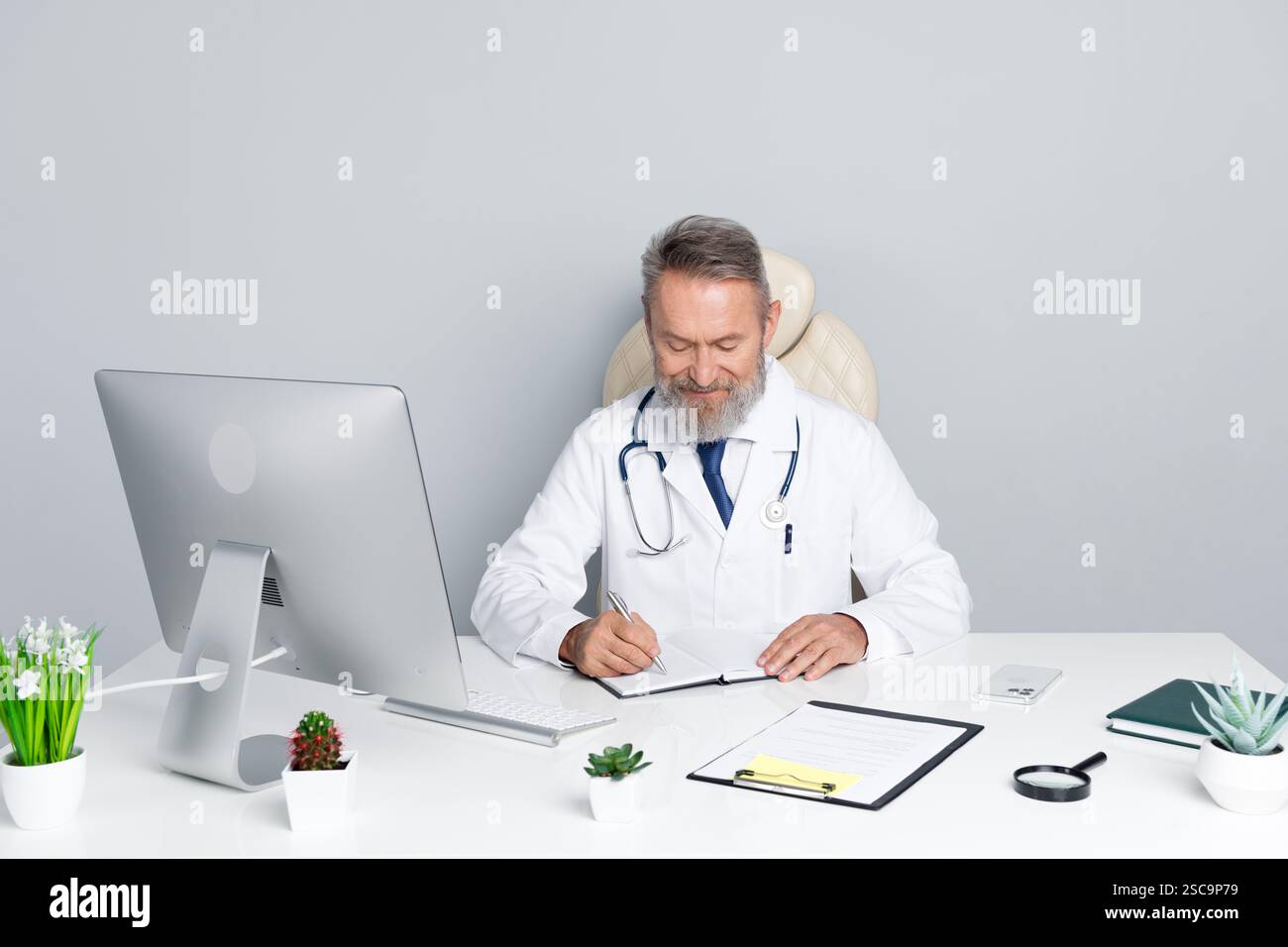 Senior male doctor working at desk completing medical paperwork in ...
