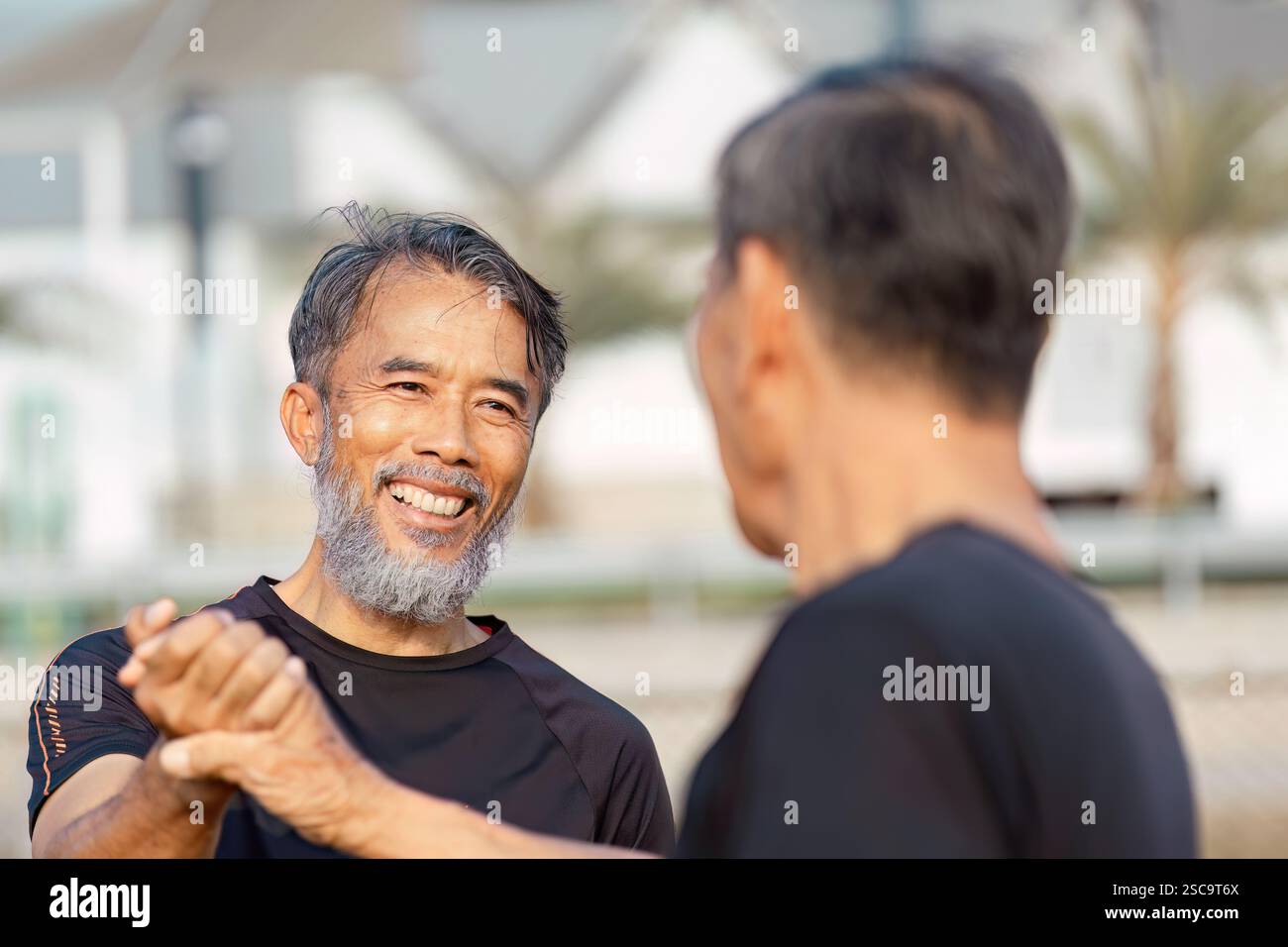 Cheerful senior Asian men sharing a handshake and laughter on a sports ...