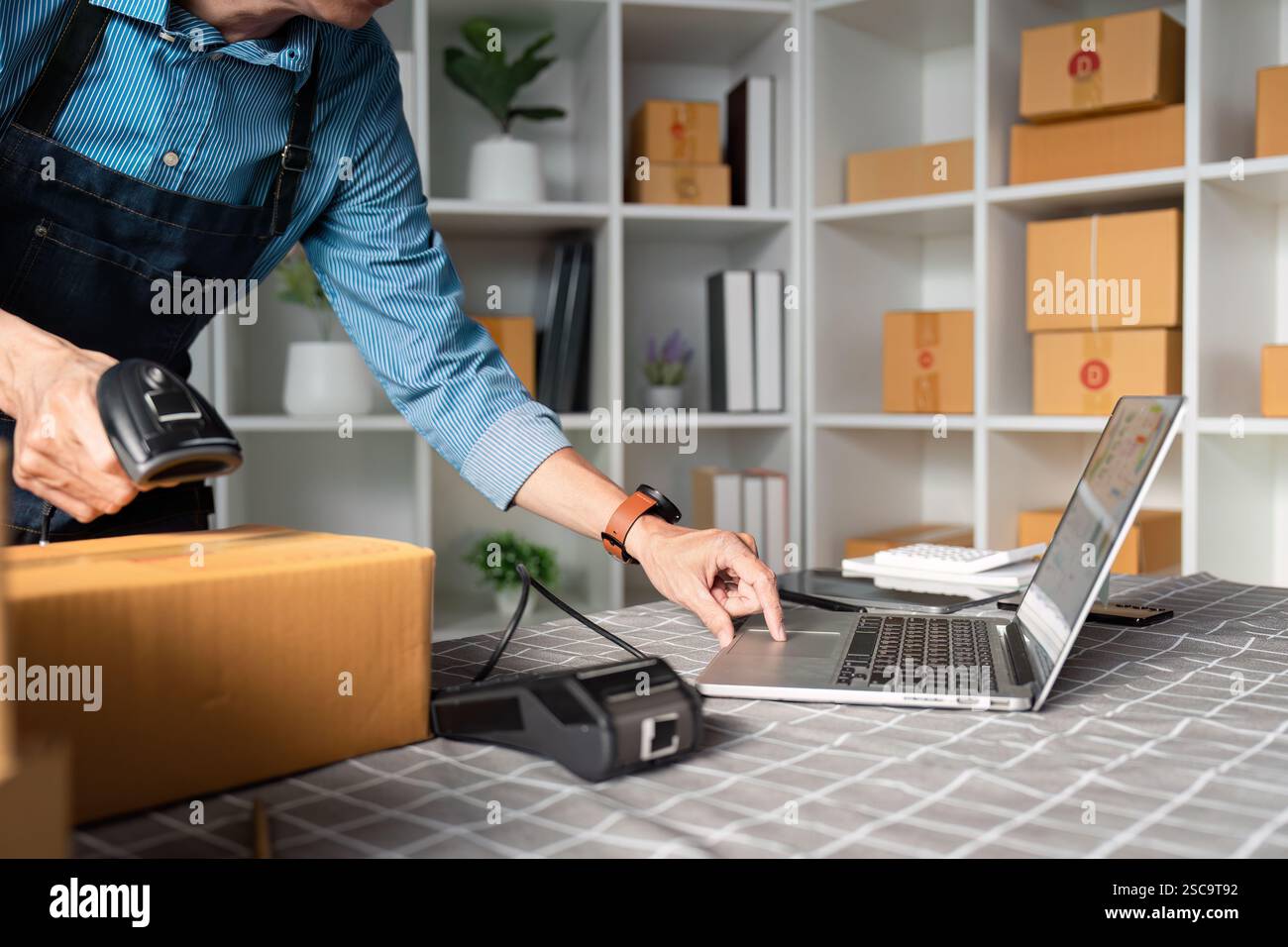 E-commerce entrepreneur using a barcode scanner and laptop to manage ...