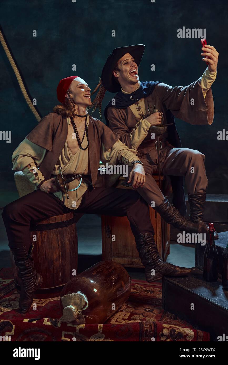 Two men, medieval pirates in bandana and hat, sitting and taking selfie ...