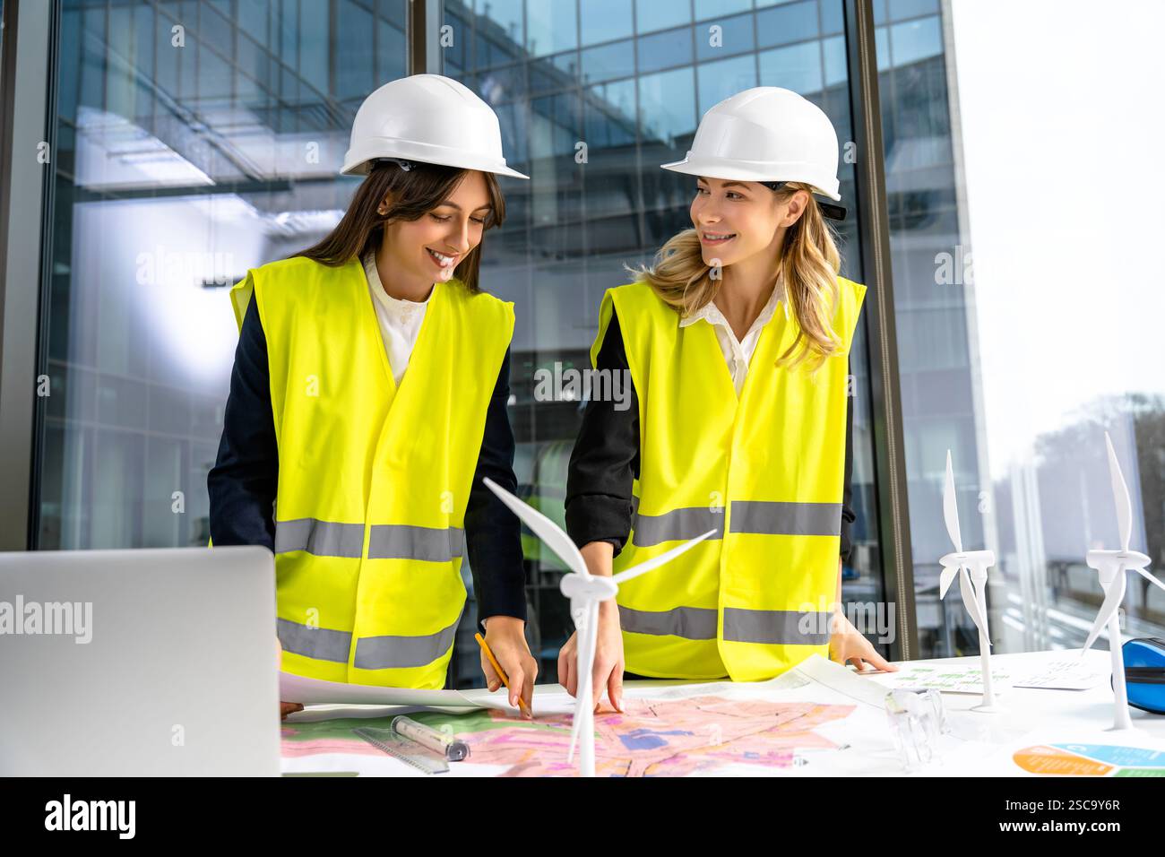 Two female engineers in yellow vest working together and looking ...