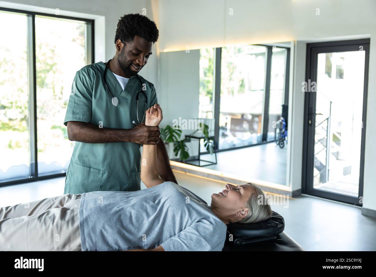 Male dark-skinned doctor working on arms stretching of his female ...