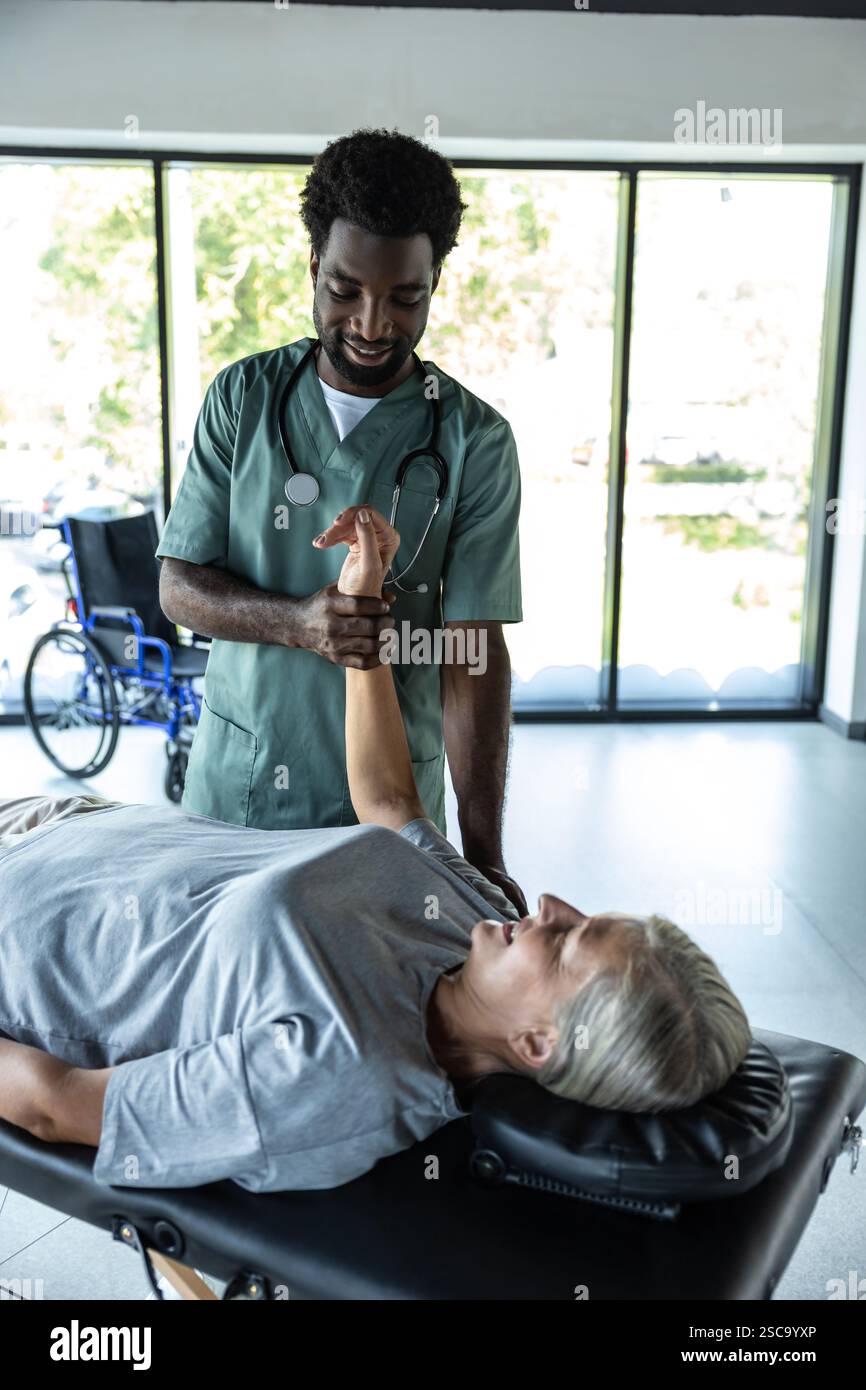 Male dark-skinned doctor working on arms stretching of his female ...