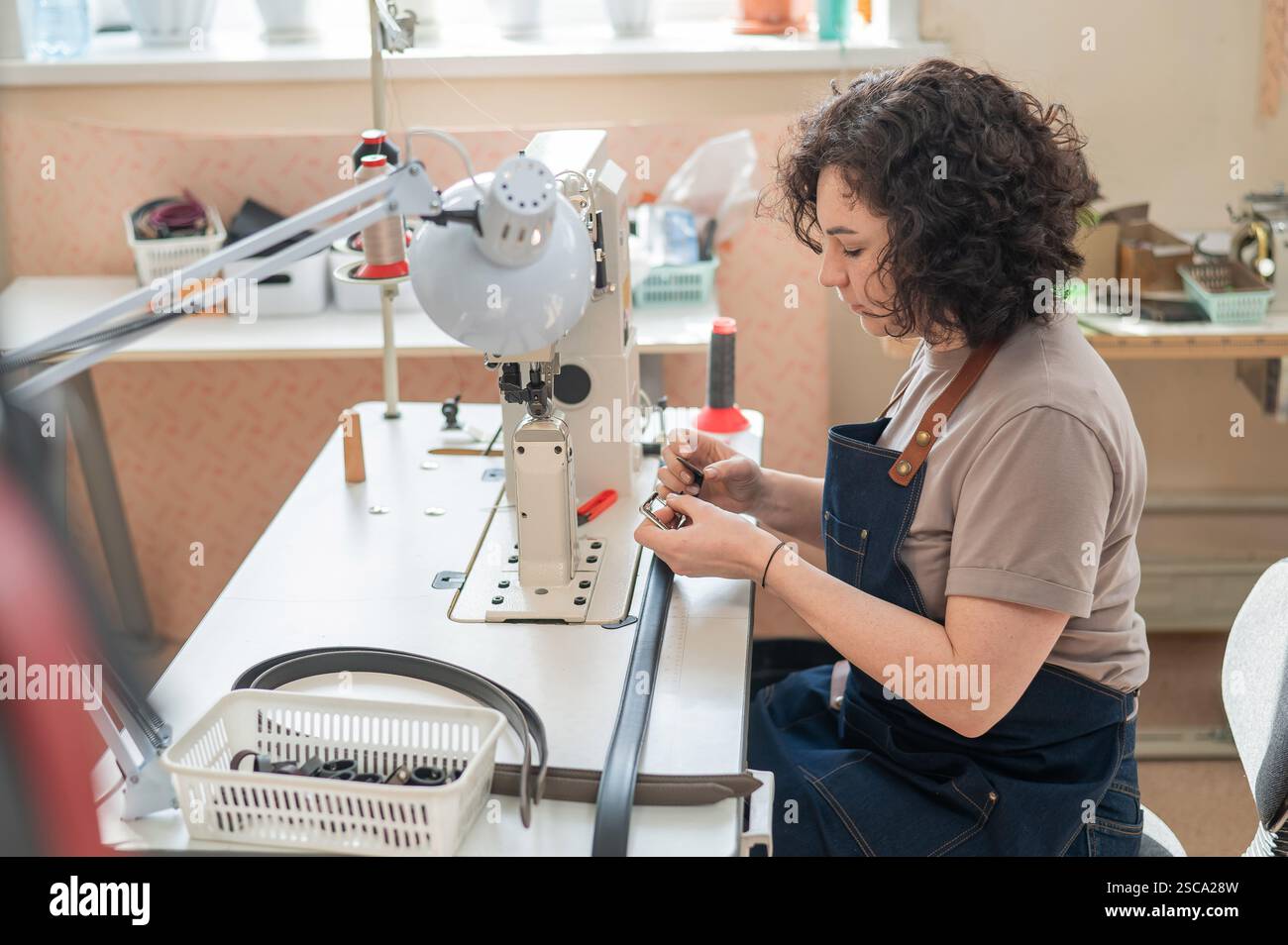A woman tanner sews a leather belt on a sewing machine Stock Photo - Alamy