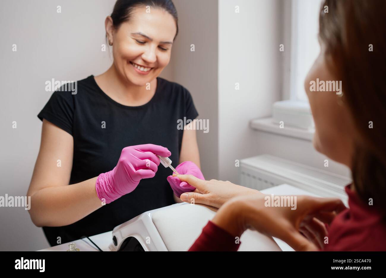 Smiling Manicure specialist female applying base nail polish. Beauty ...