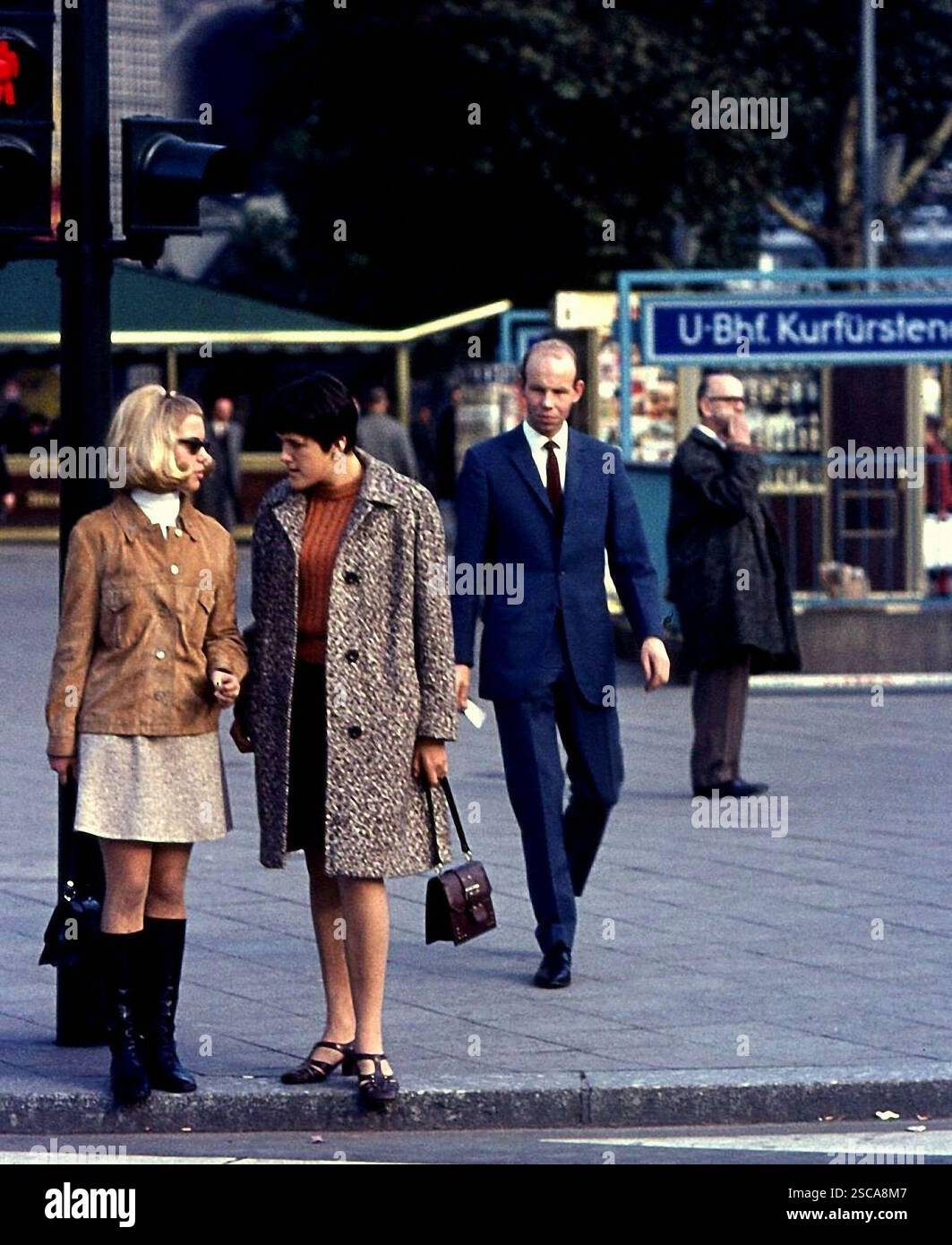 Women with skirt, coat, sunglasses and handbag and a man wearing a suit ...