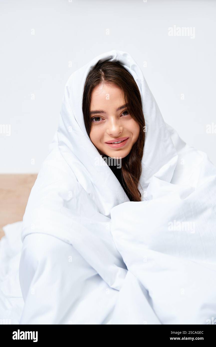 A beautiful young woman smiles gently while draped in soft, cozy white ...