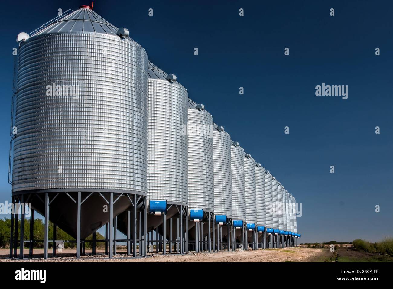 A row of large metal tanks are lined up in a field. The tanks are ...