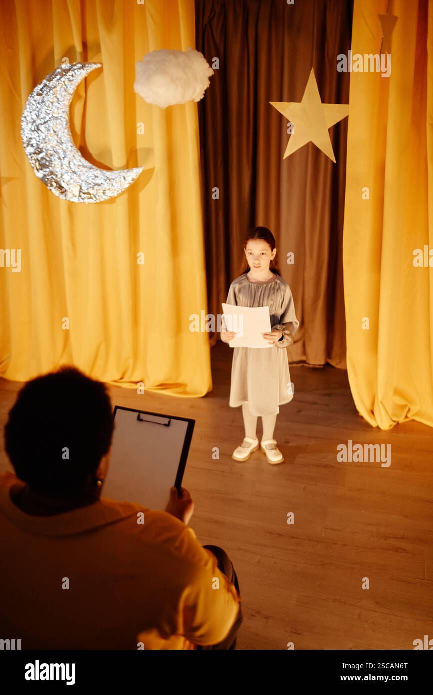 Little girl reciting lines from paper while surrounded by stage decor ...