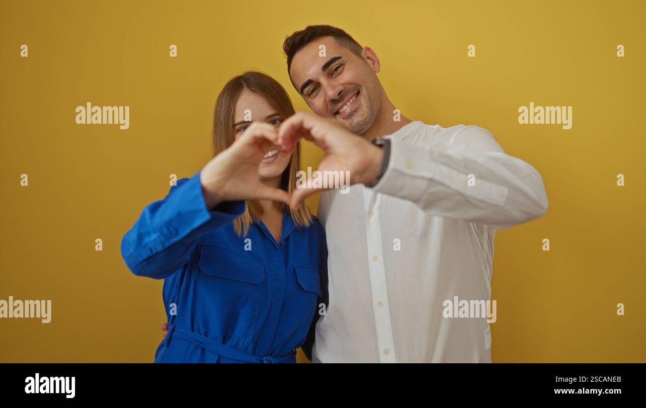 Couple smiling and forming heart shape with hands on yellow background ...