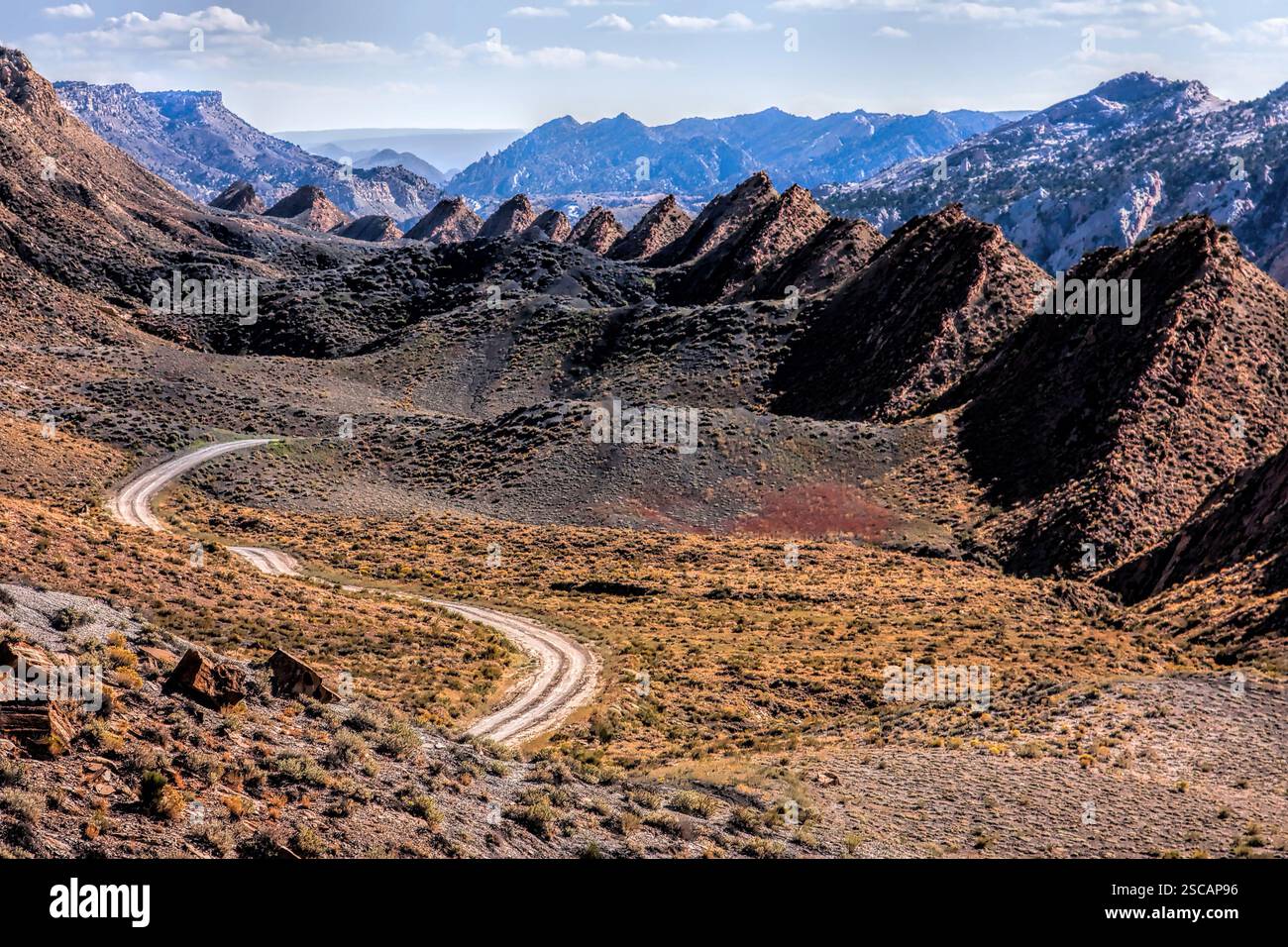 A road winds through a desert with mountains in the background. The ...