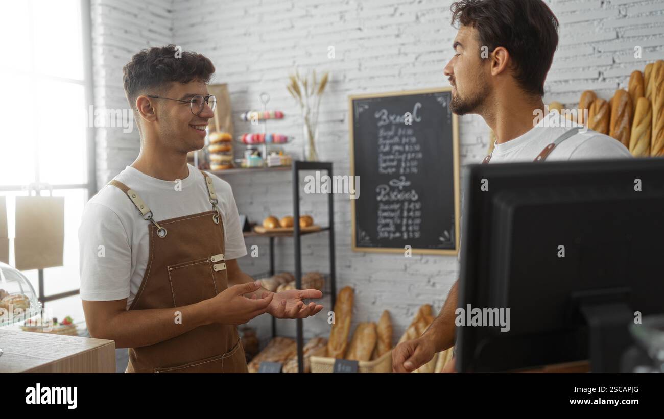 Two hispanic male bakery workers conversing indoors in a shop, with ...