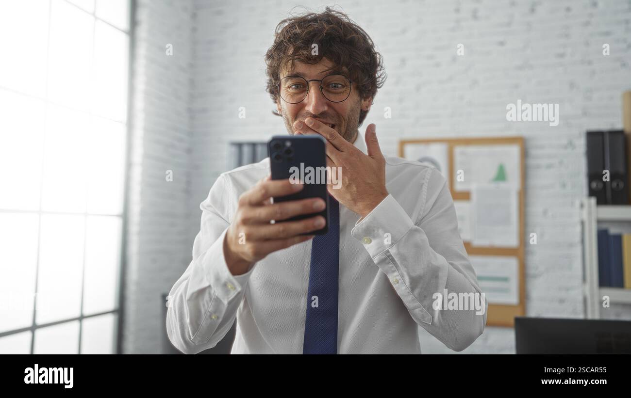 Young man in an office smiles at his smartphone displaying a joyful ...