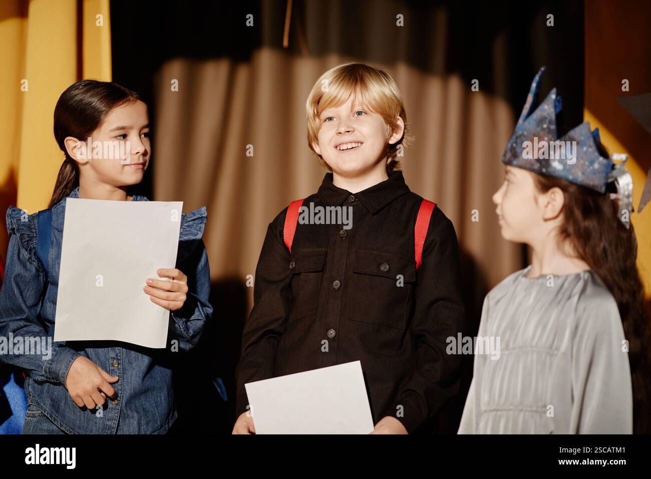Three children on stage during school theater performance. Smiling boy ...