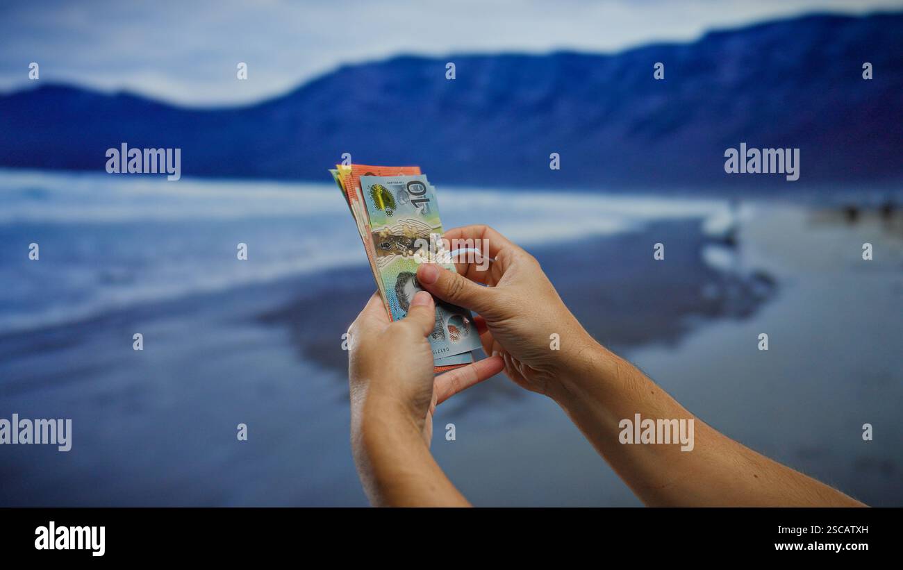 Hands holding australian dollar banknotes on a beach, symbolizing ...