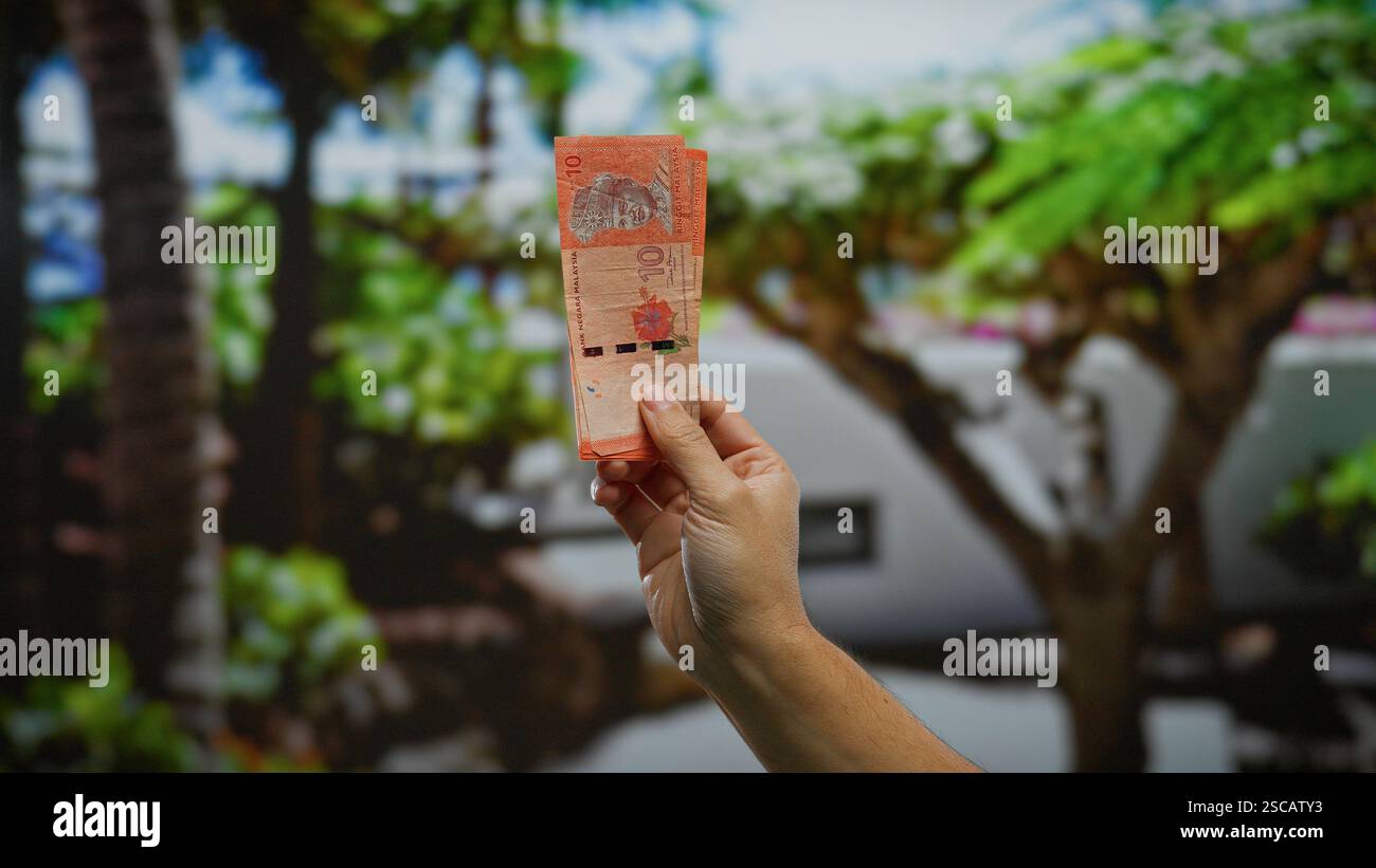 Man holding malaysian ringgit banknotes outdoors in a vibrant urban ...