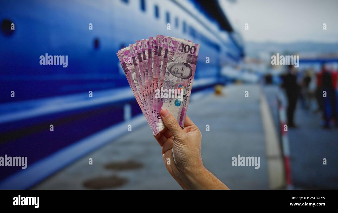 Hand holding philippine pesos showing money by a seaside town port with ...